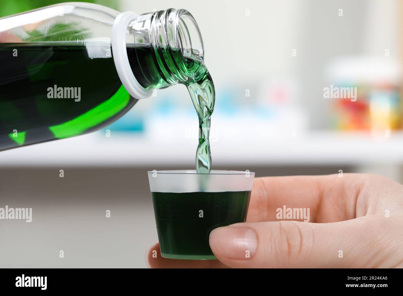 Woman pouring syrup from bottle into measuring cup against blurred ...