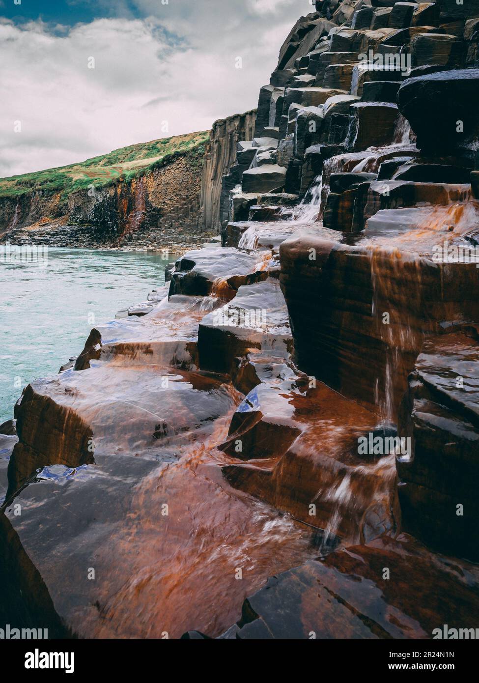 A vertical shot of water flowing over hexagonal rock formations in the ...