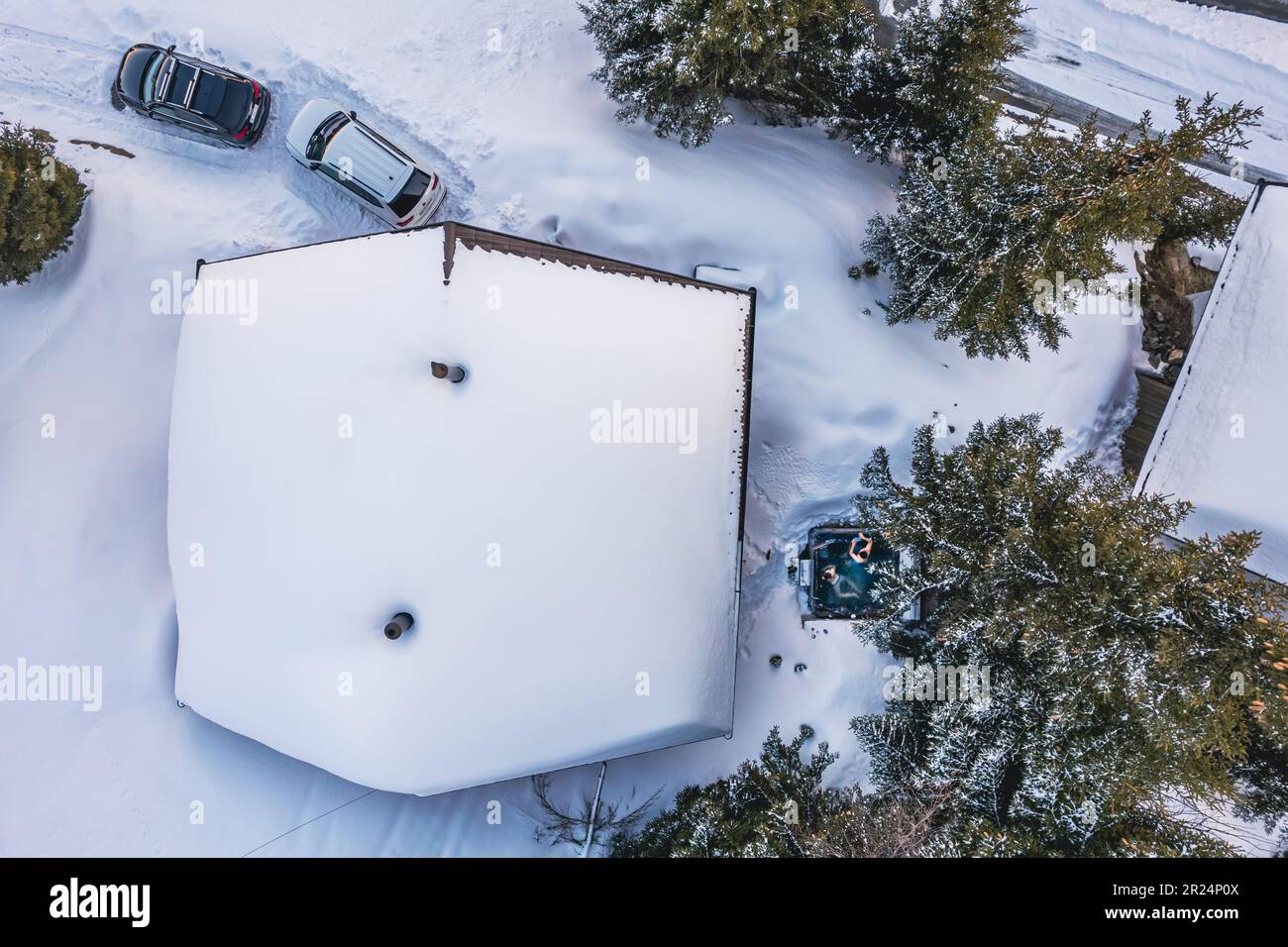An aerial view of a house covered in snow and two cars in its driveway ...