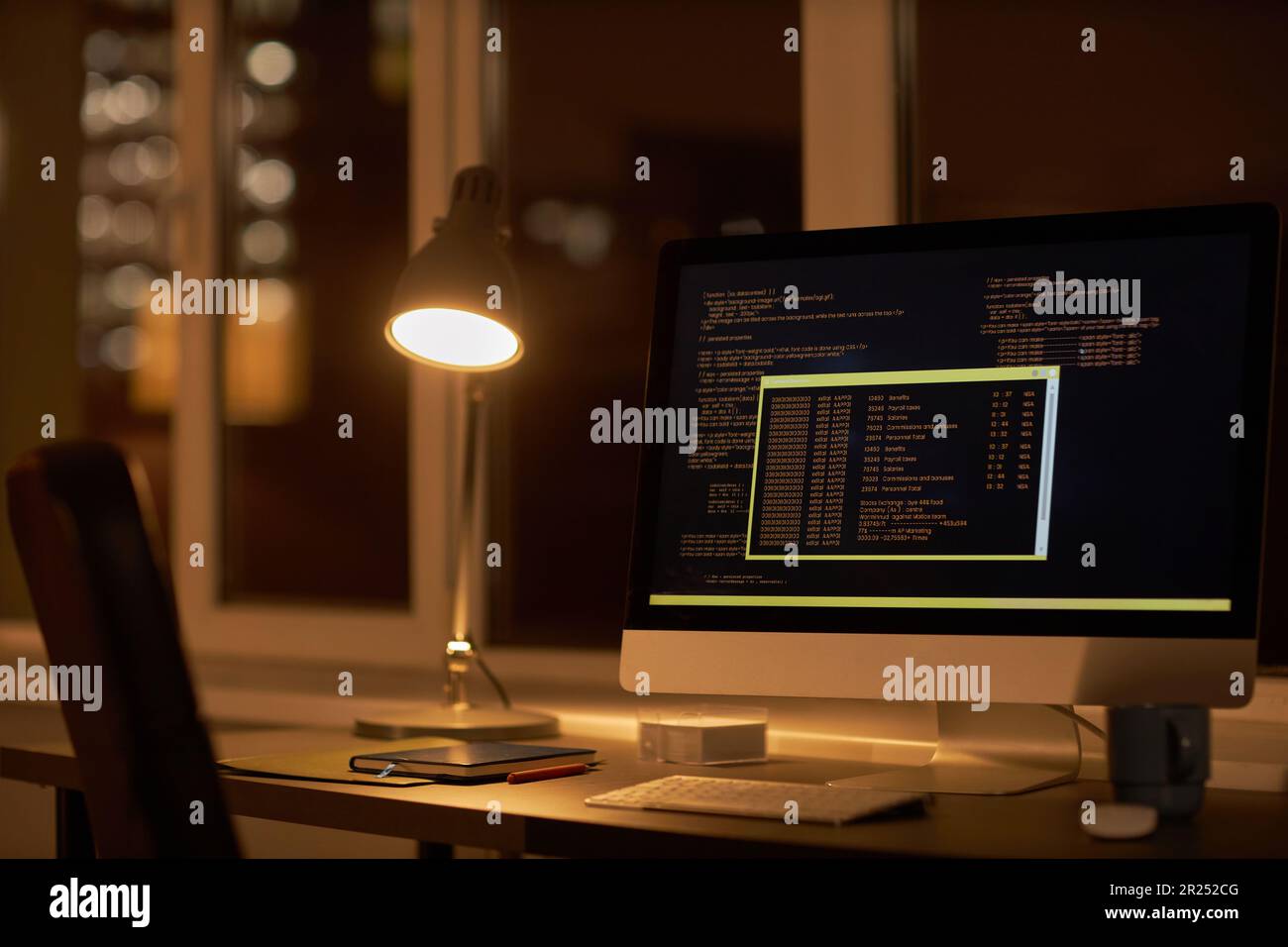 Close-up of workplace of developer with computer with security codes on monitor in dark office ...