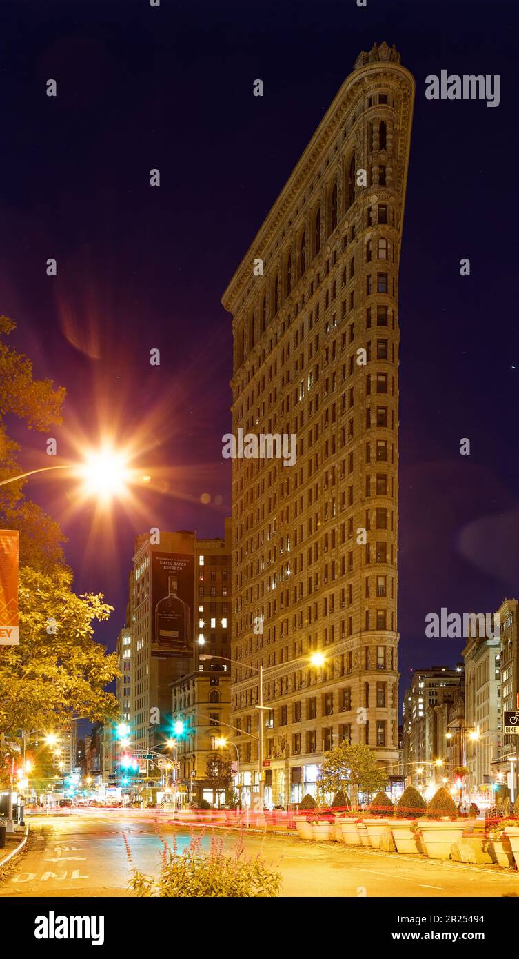 The Flatiron Building glows warm under streetlights under an indigo pre ...