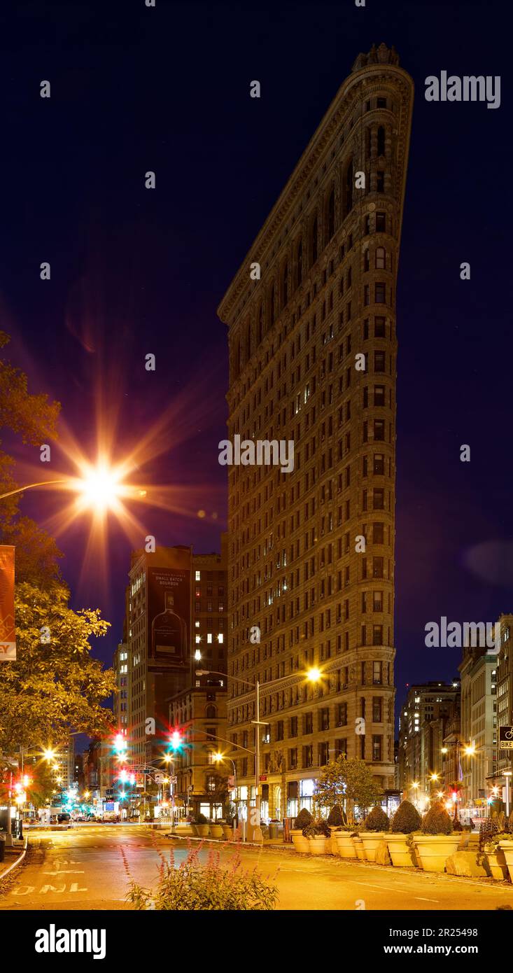 The Flatiron Building glows warm under streetlights under an indigo pre ...
