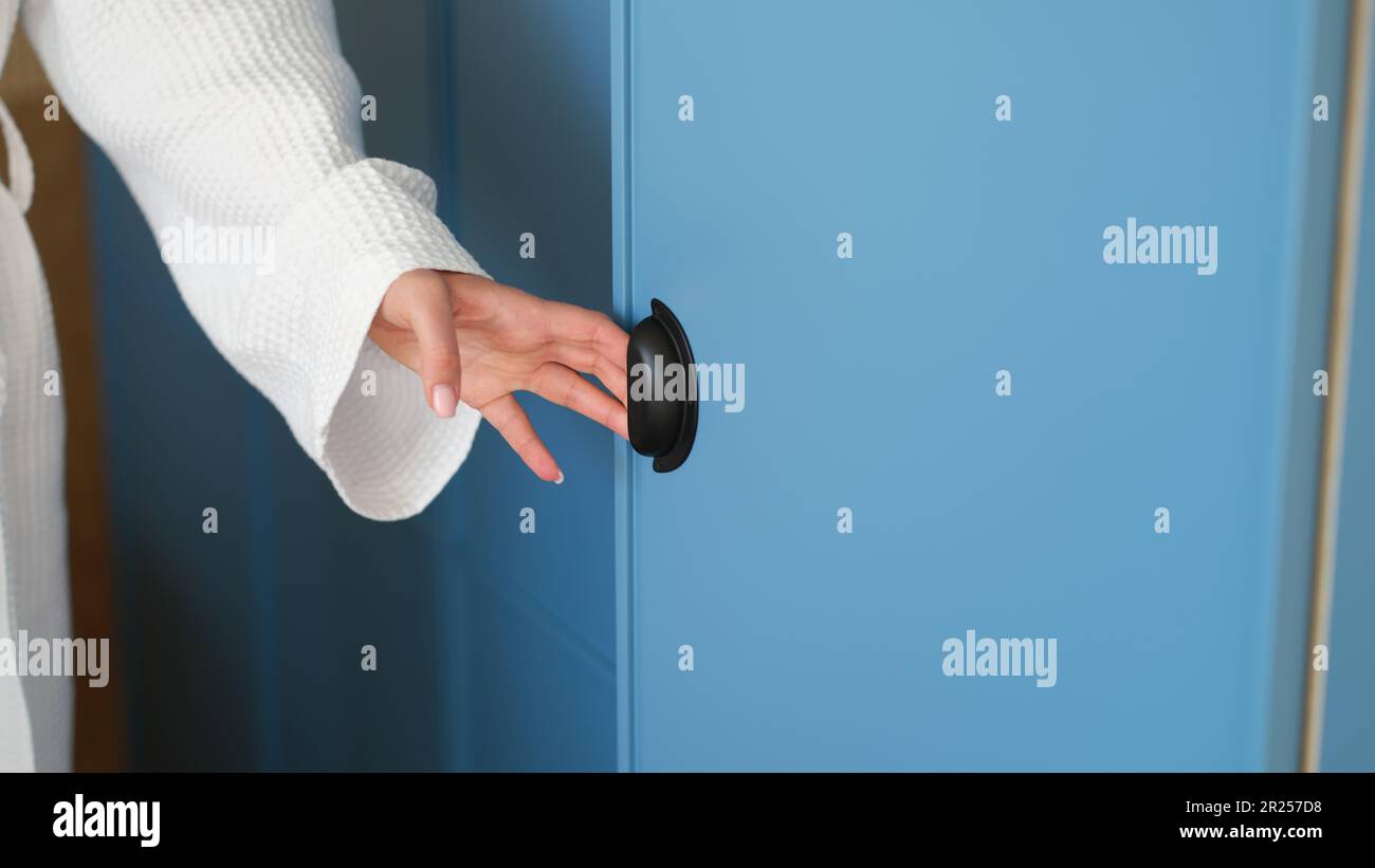 Woman in white bathrobe opening door of blue wardrobe in hotel with ...