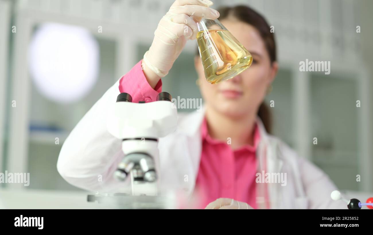 Scientist chemist looking at flask with yellow liquid or oil for ...