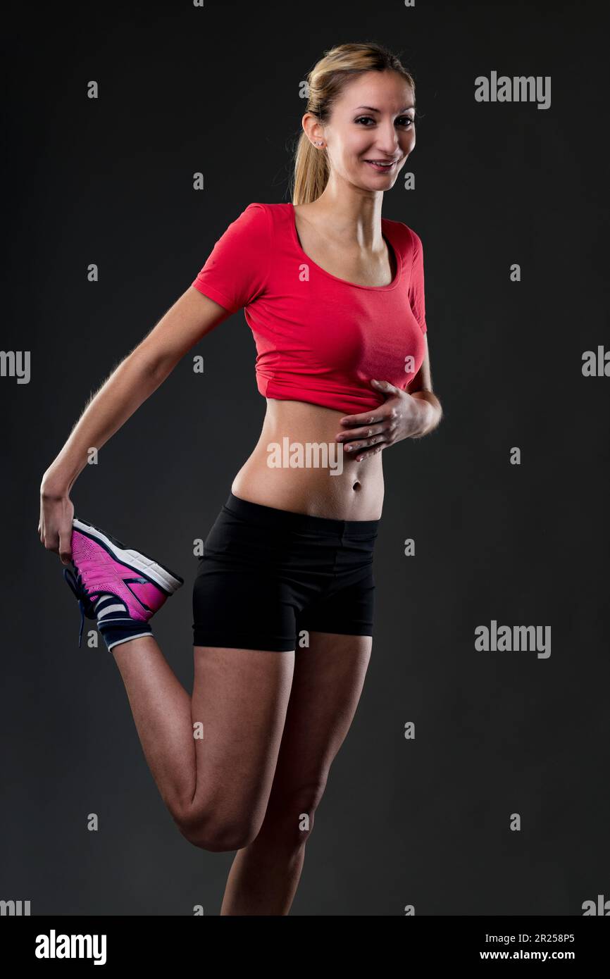 One-legged stretch by woman in red top, black mini pants, pink sneaker ...