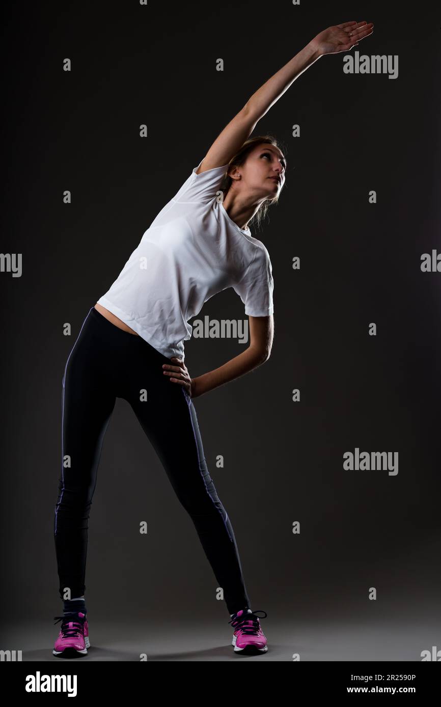 Blonde woman exercising, on black background, wearing dark fitting ...