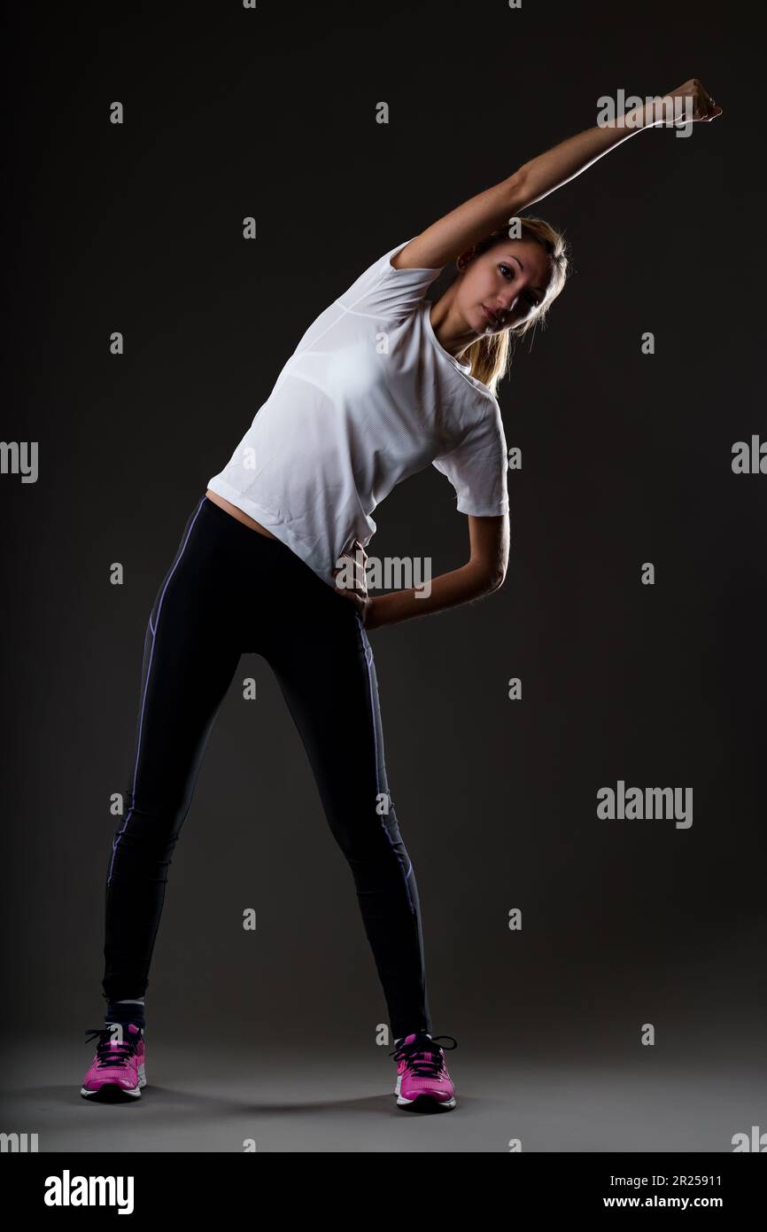 Blonde woman exercising, on black background, wearing dark fitting ...