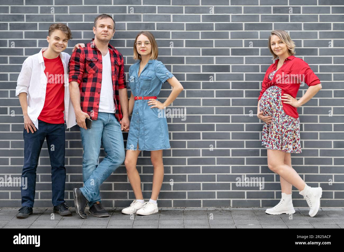 Pregnant woman with her happy family stands near brick wall. Mother ...