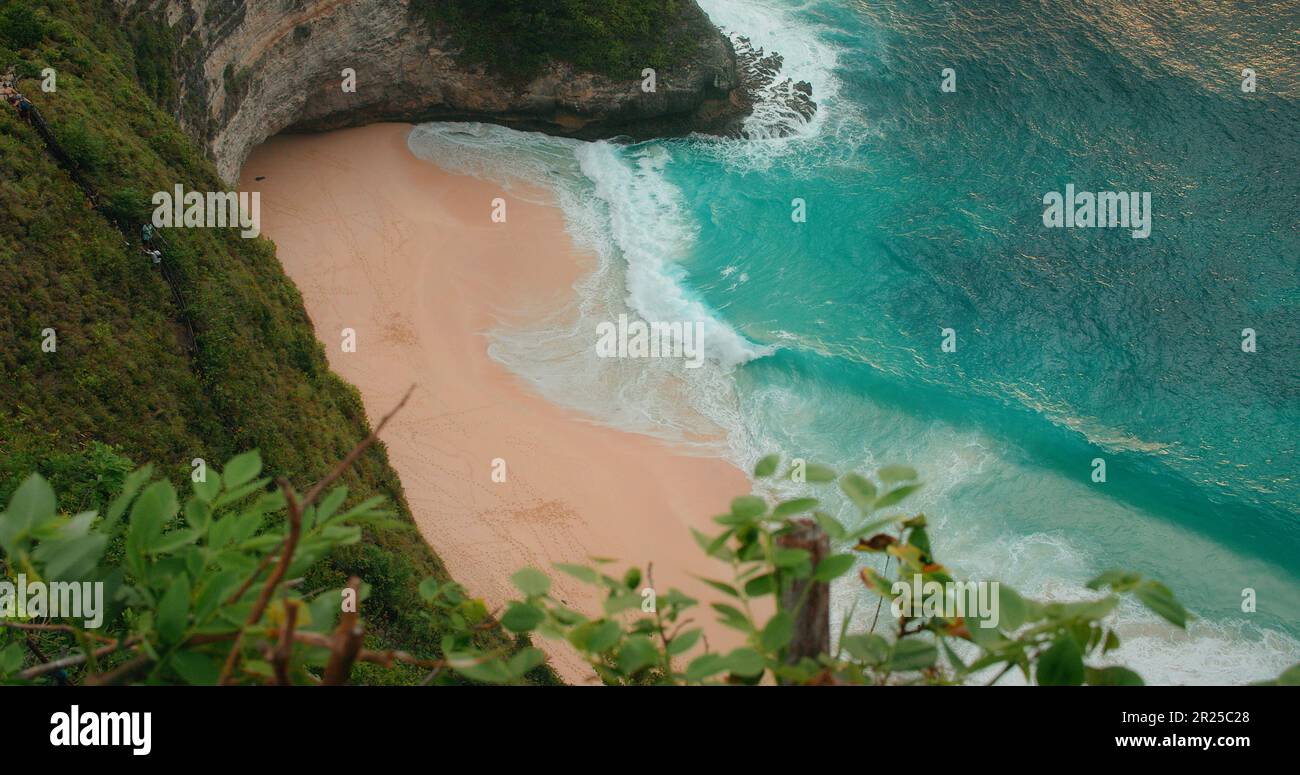 Turquoise ocean waves roll on golden sandy Kelingking beach at sunset ...