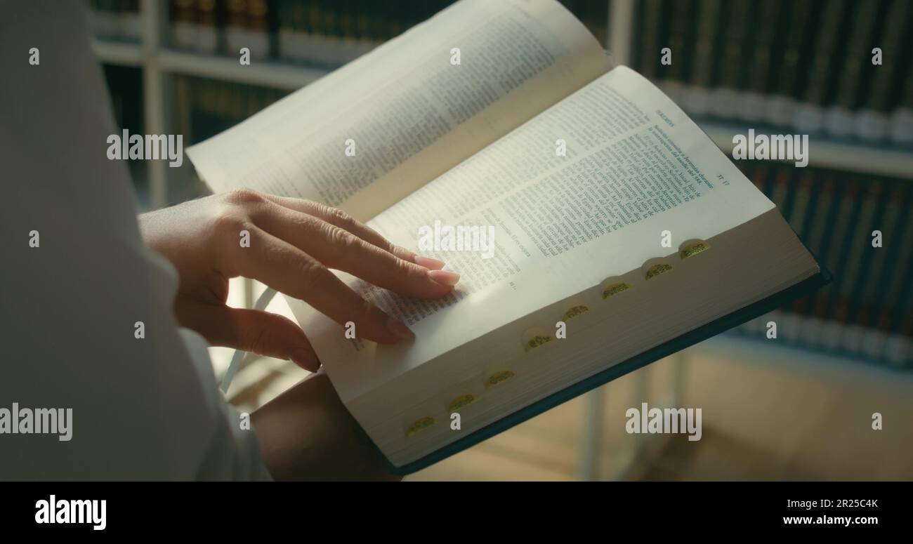 Close-up female hands holding and reading a book in public library ...