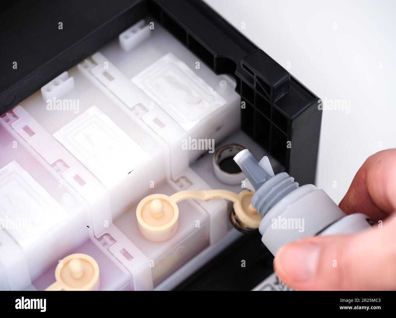 Woman hand holding the bottle with black colour ink refilling printer ...