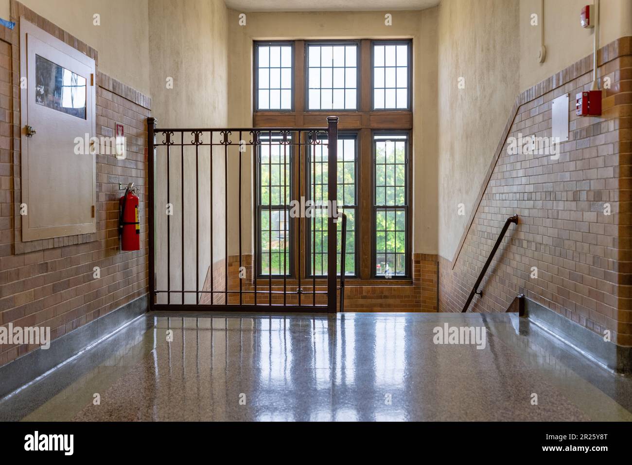 Nondescript stairway, hallway, with windows and brown railing, in a ...
