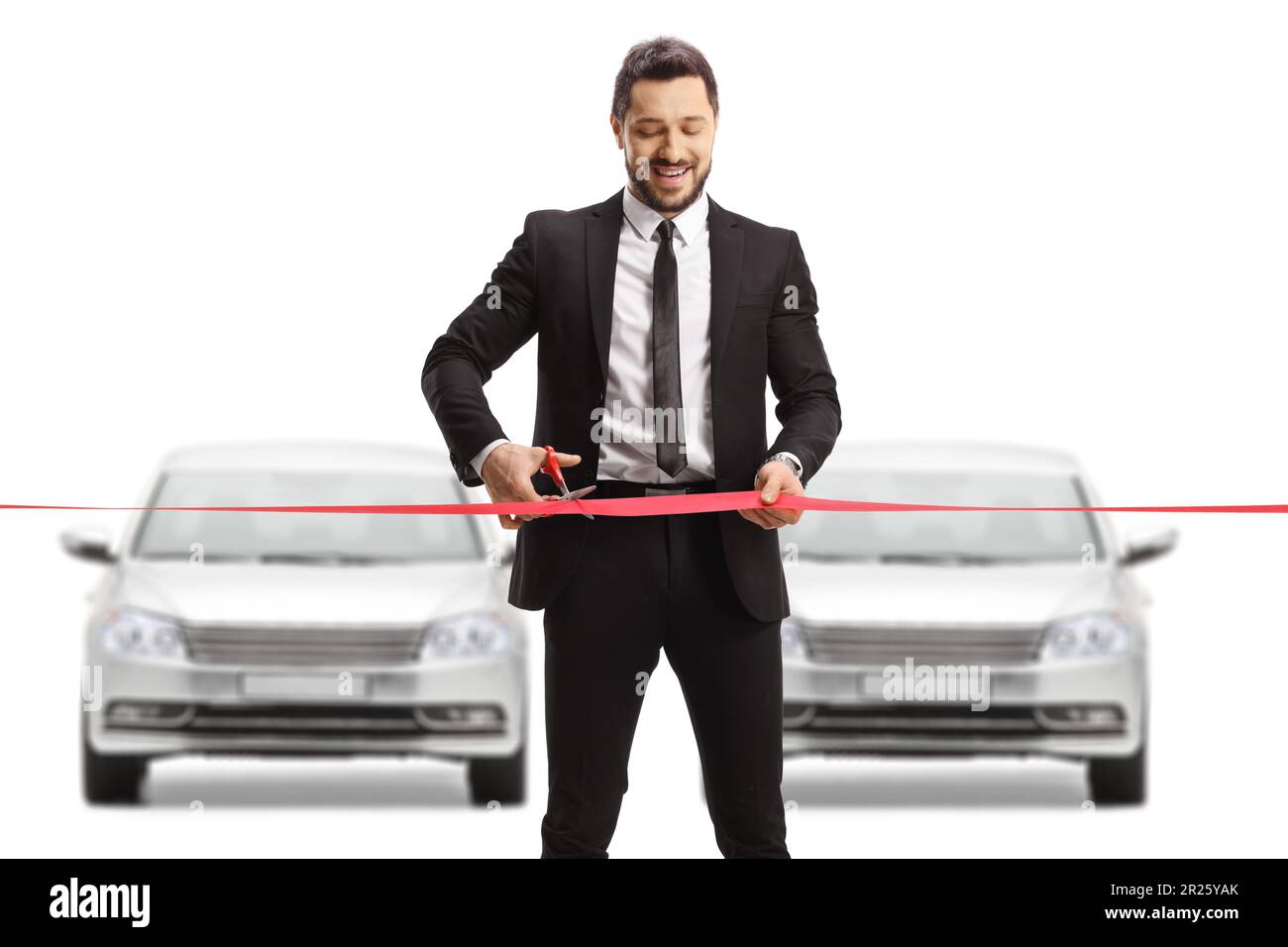 Businessman cutting a red ribbon tape in front of a row of silver cars ...
