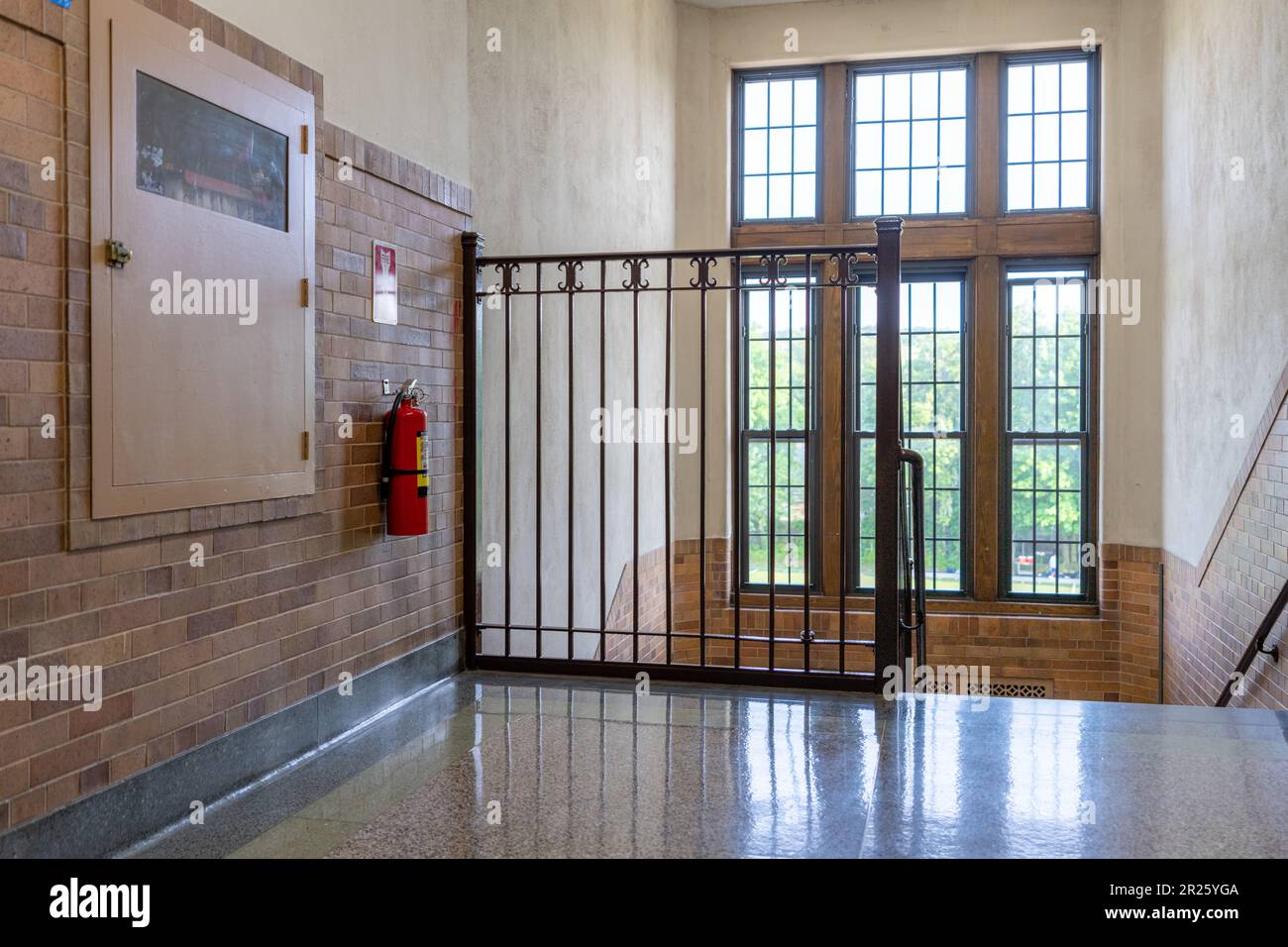 Nondescript stairway, hallway, with windows and brown railing, in a ...