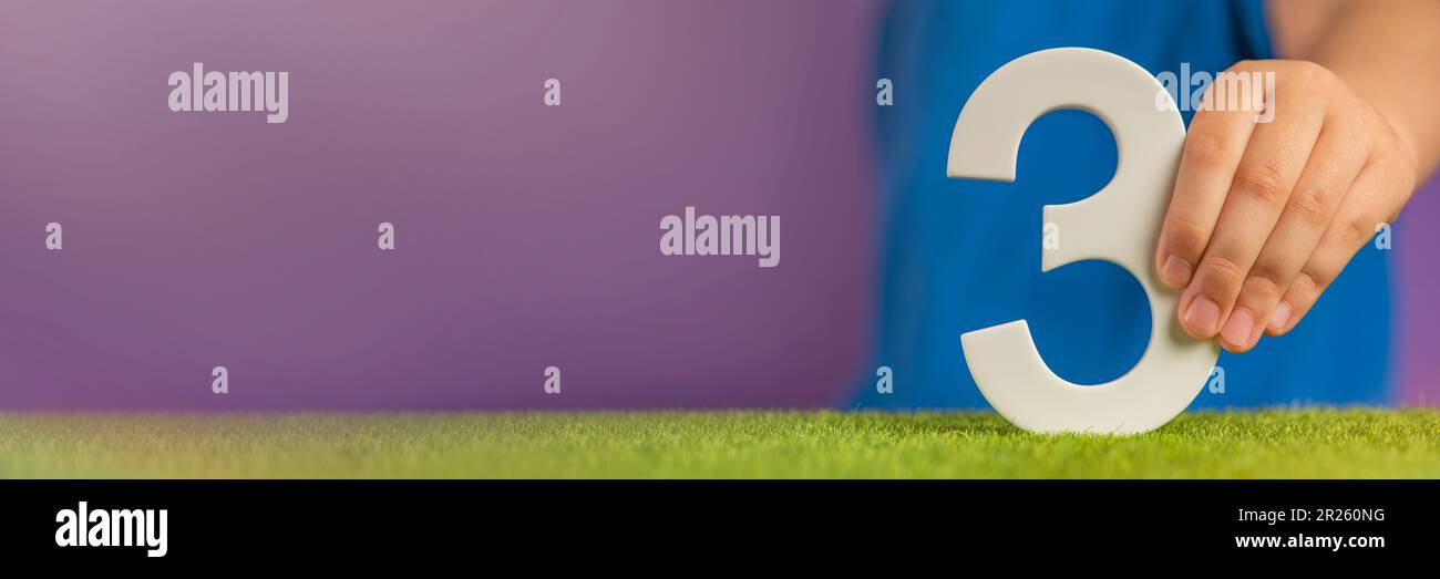 Number 3 in hand. Hand holding white number three over green grass and ...