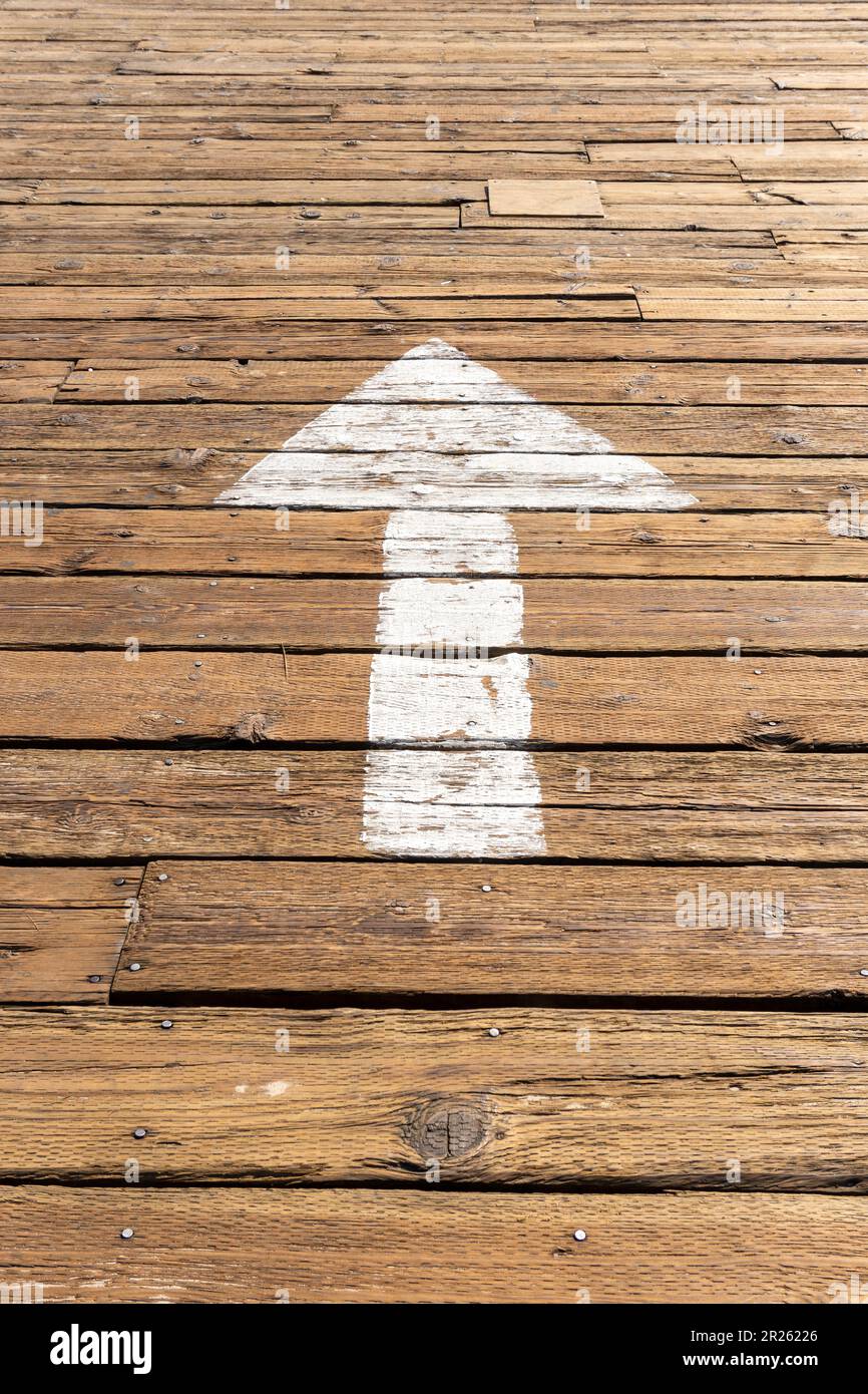 A white painted arrow sign on a weathered wooden pier deck Stock Photo ...