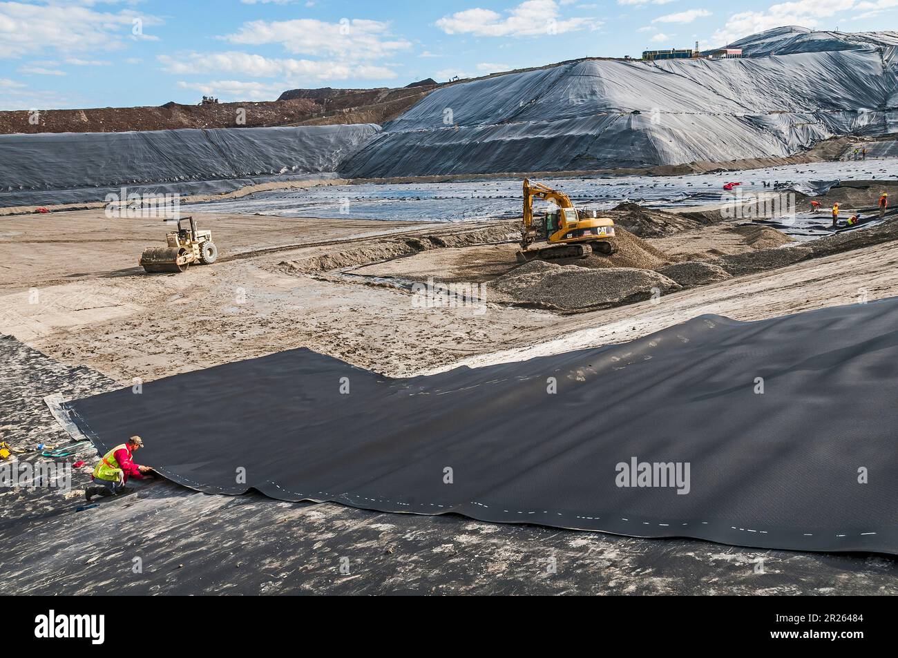 Workers, a power shovel, and a compaction roller are in an active ...