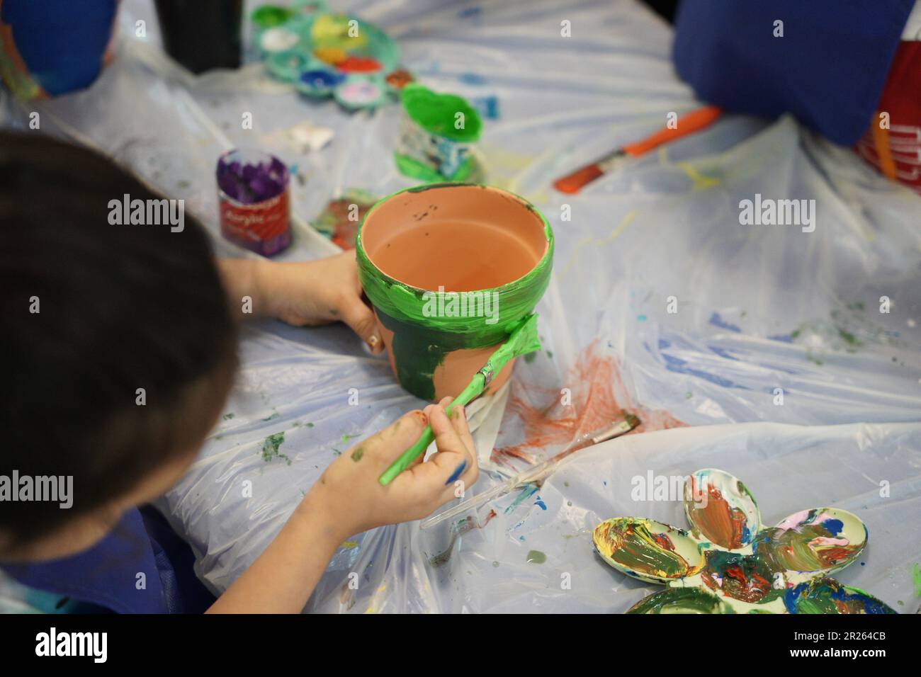 Little kid colouring a pot with messy green colo. A kid holding a pot ...