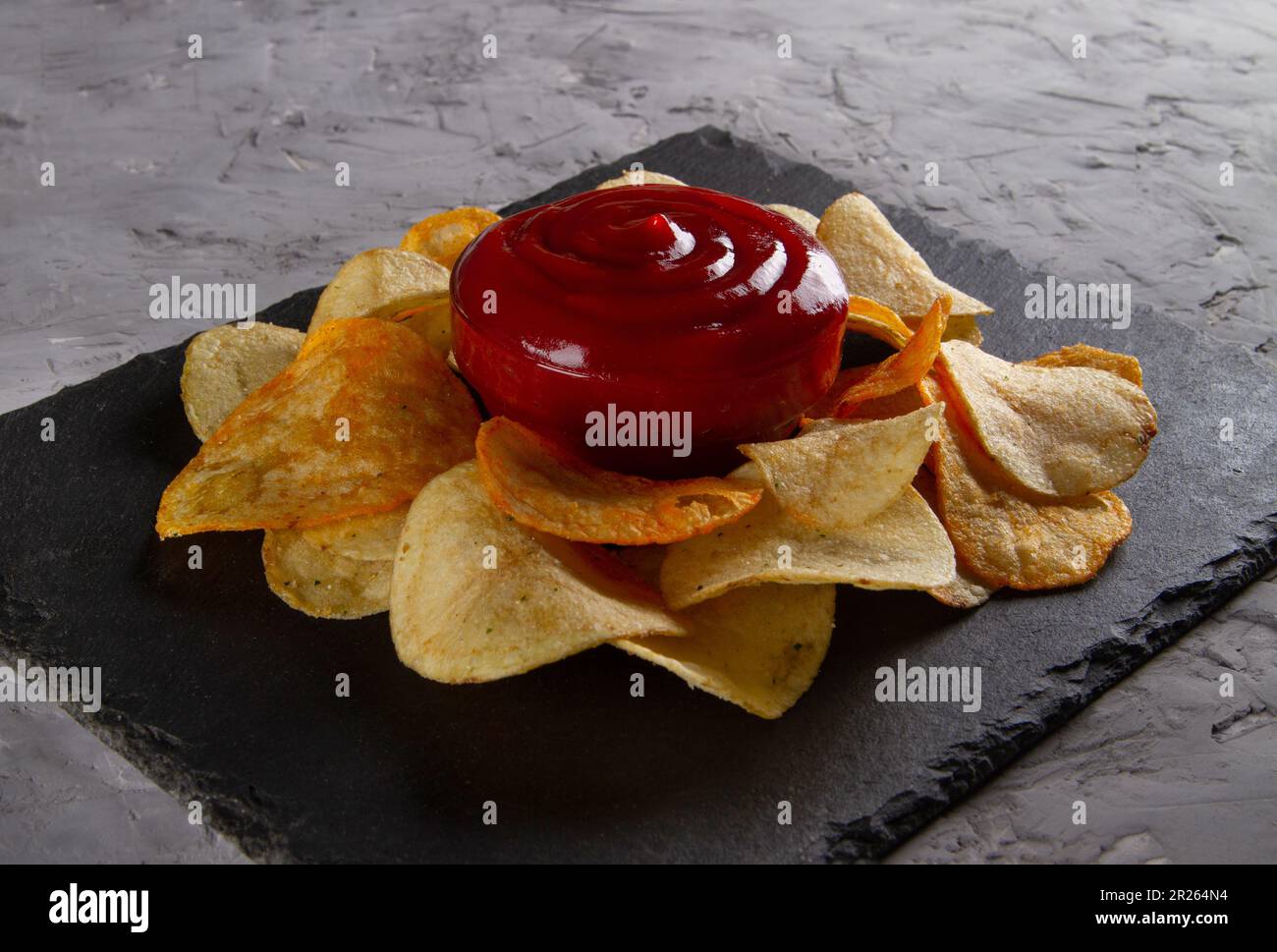 Side view of heap of potato chips with red dipping sauce on black slate ...