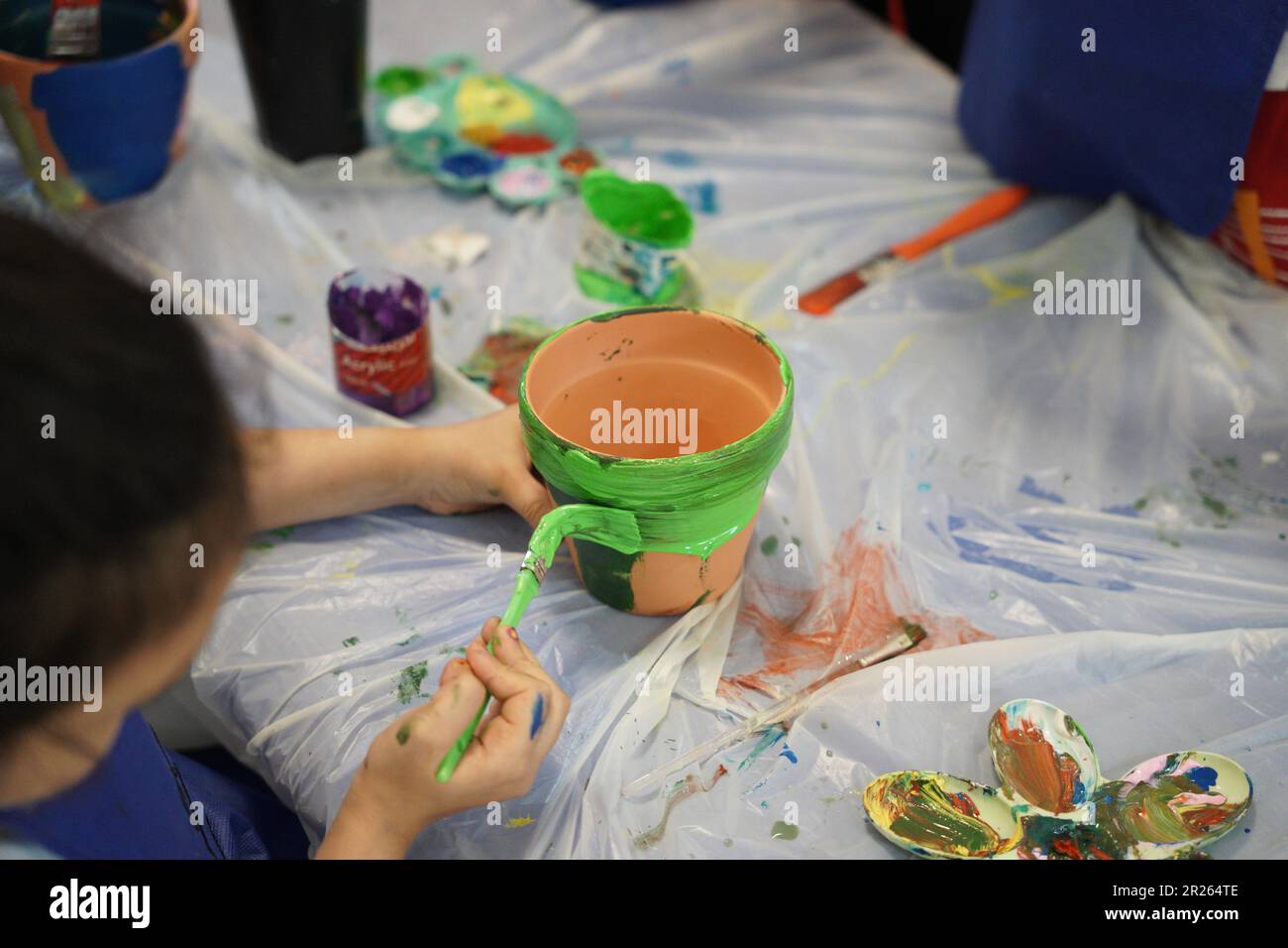 Little kid colouring a pot with messy green colo. A kid holding a pot ...