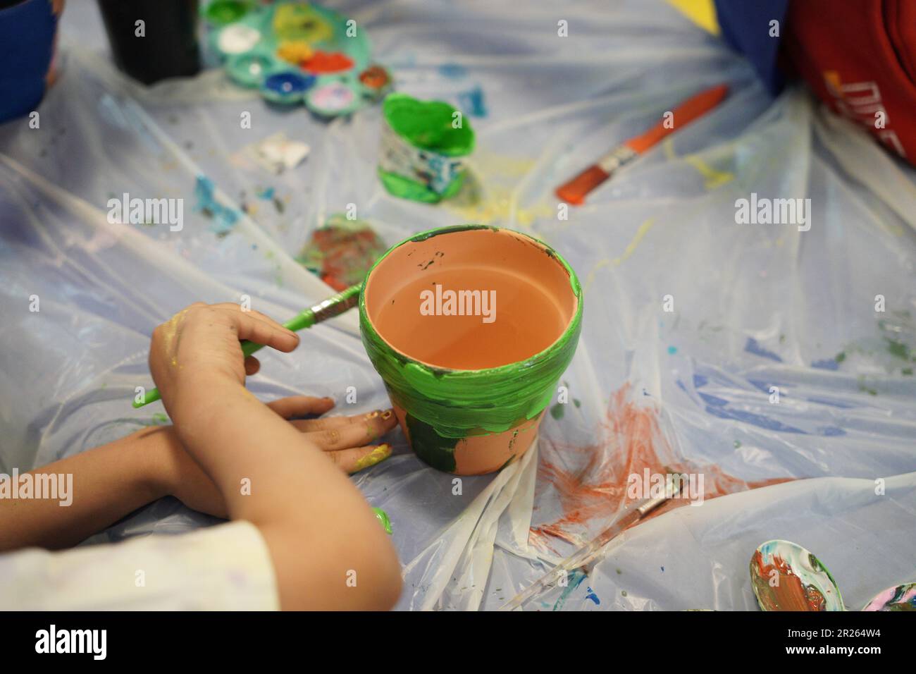 Little kid colouring a pot with messy green colo. A kid holding a pot ...