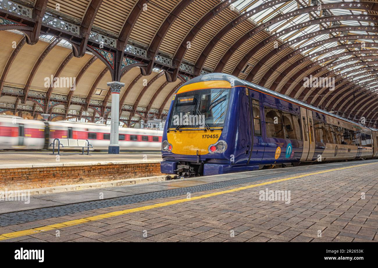 A train stands beside a platform and under a historic iron and curving ...