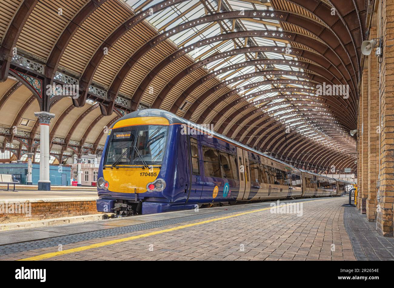 A train stands beside a platform and under a historic iron and curving ...