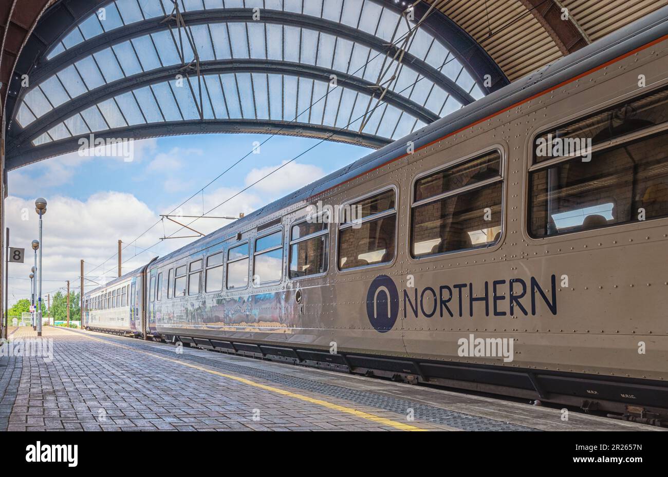 A train stands beside a platform and a historic iron and glass arch ...