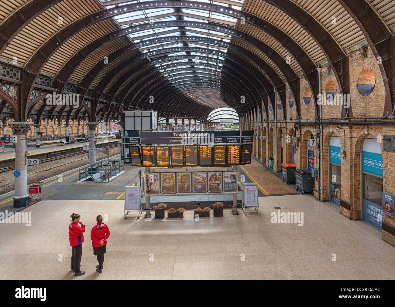 A station concourse with an electric timetable. Two crew members stand ...