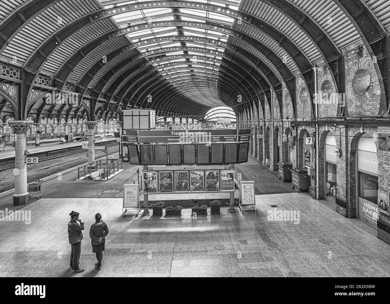 A station concourse with an electric timetable. Two crew members stand ...