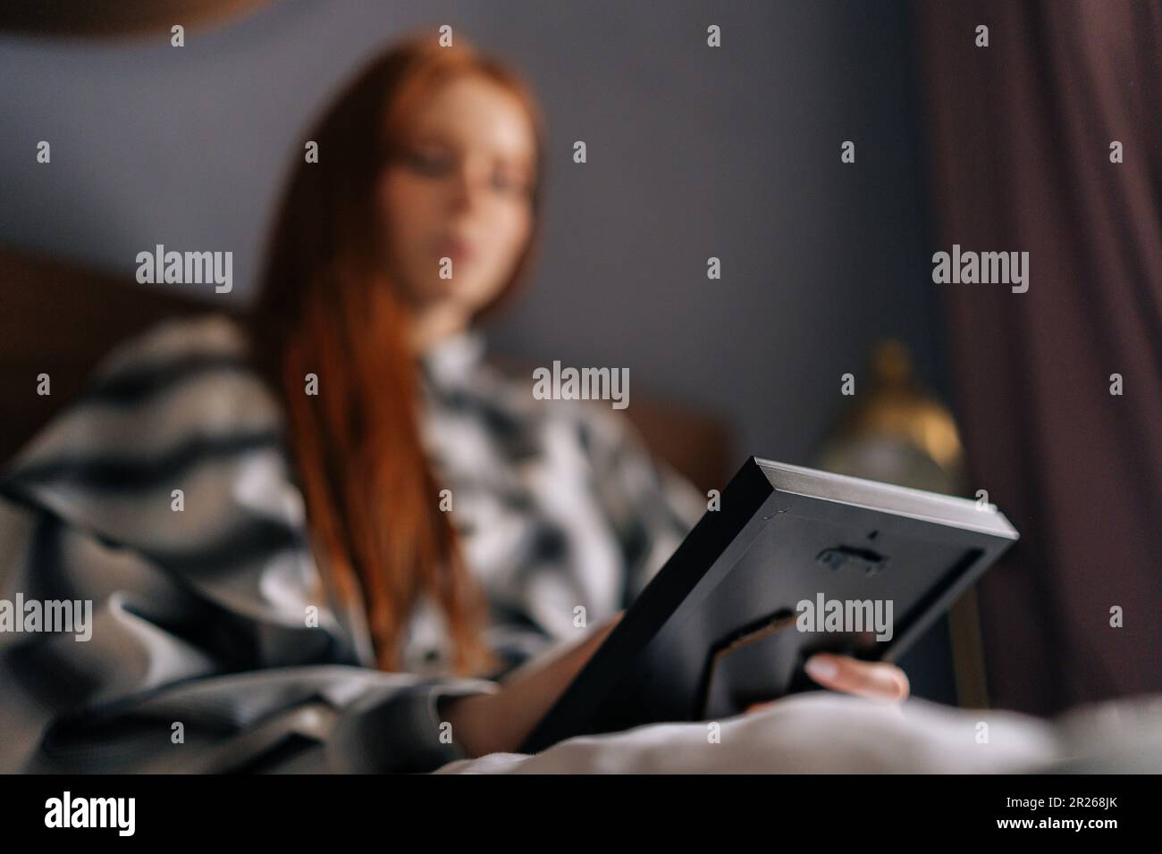 Closeup selective focus shot of sad young woman lying on bed holding ...