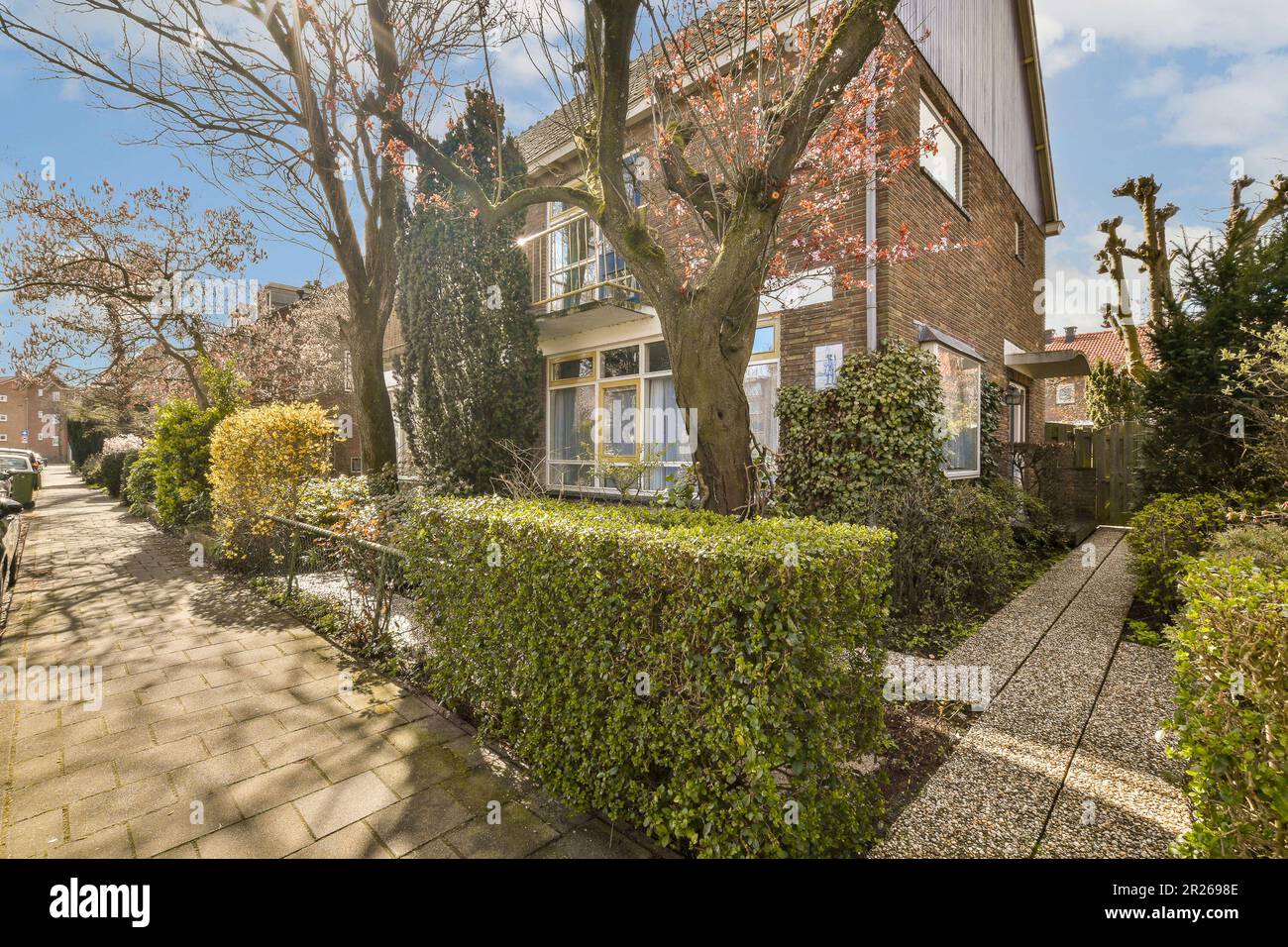 a house with trees in the front yard and bushes growing on the sidewalk ...