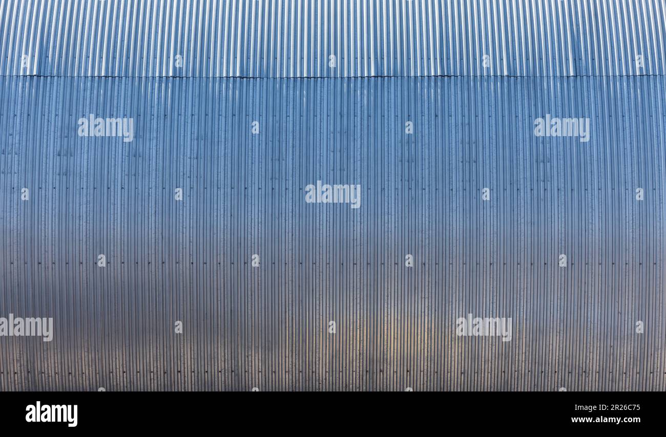 Shiny bent ridged metal wall of a storage building, modern industrial ...