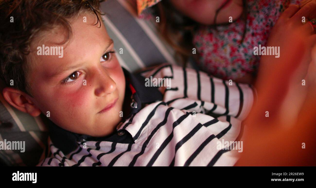 Child staring at screen at night holding tablet device watching content ...