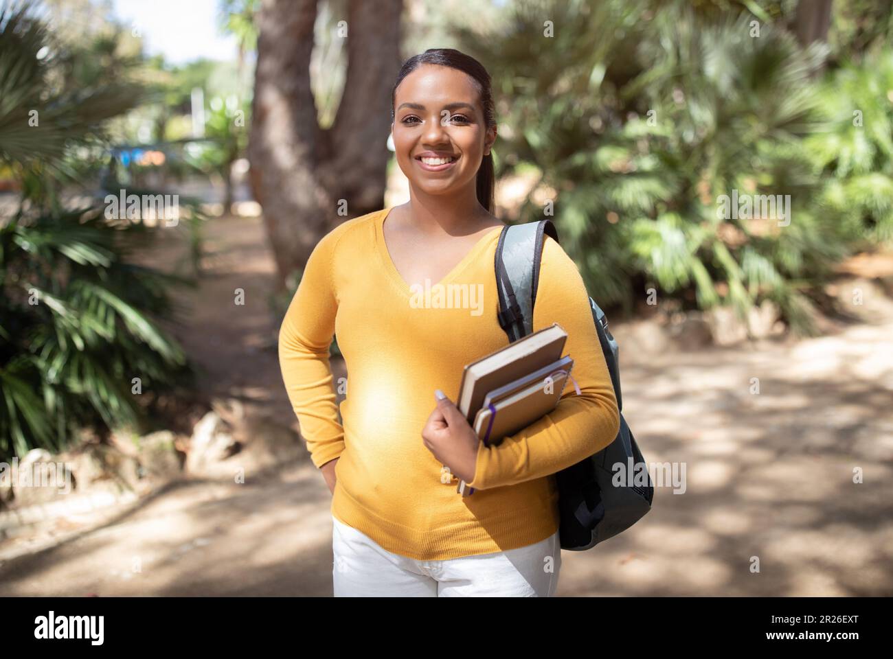 Smart brazilian student lady with backpack holding books, smiling at ...