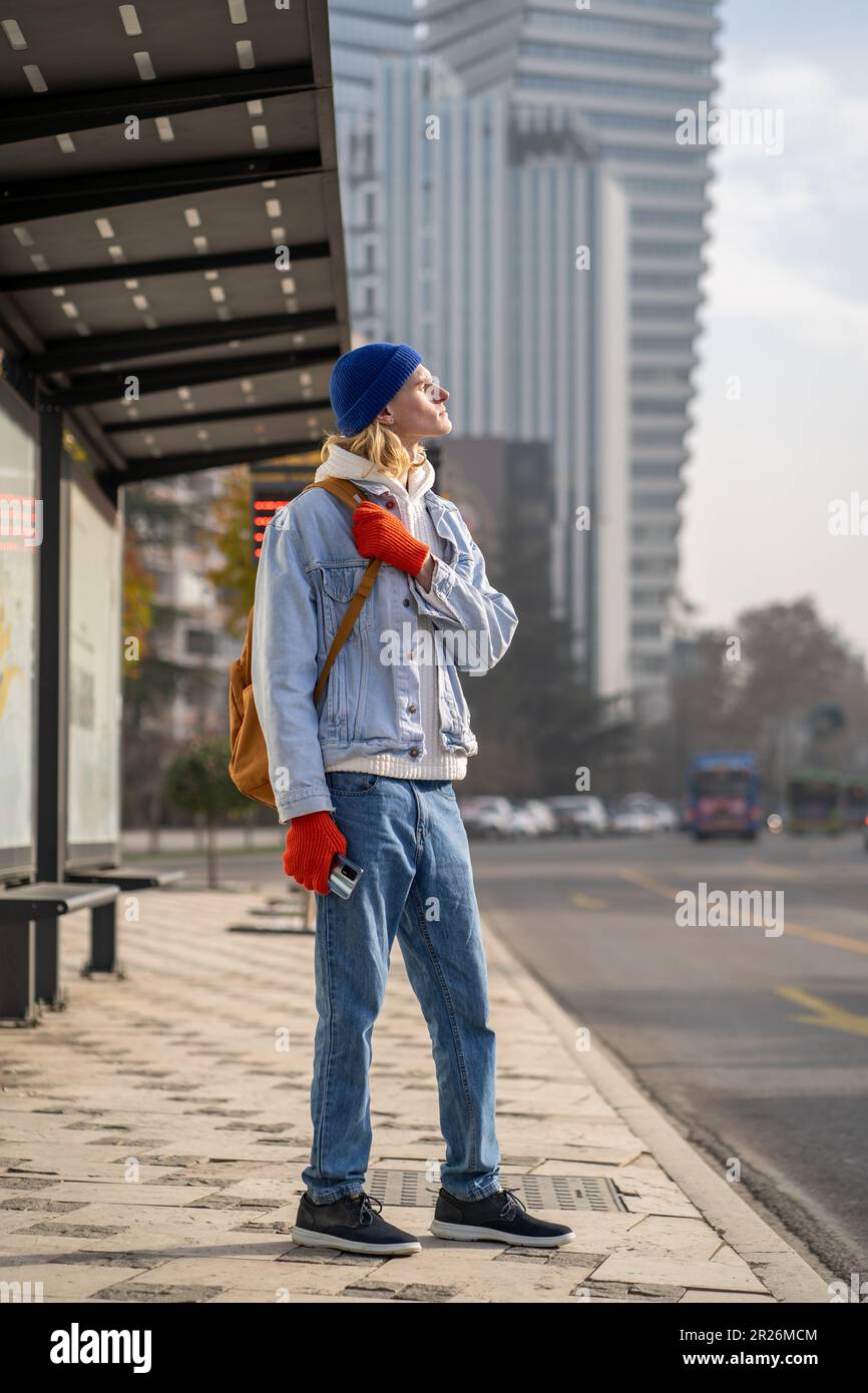 Teen boy with backpack standing alone at bus stop enjoying sunny ...