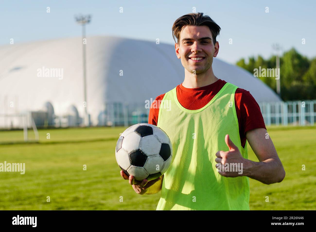 Young smiling man football player holding soccer ball with thumb up ...