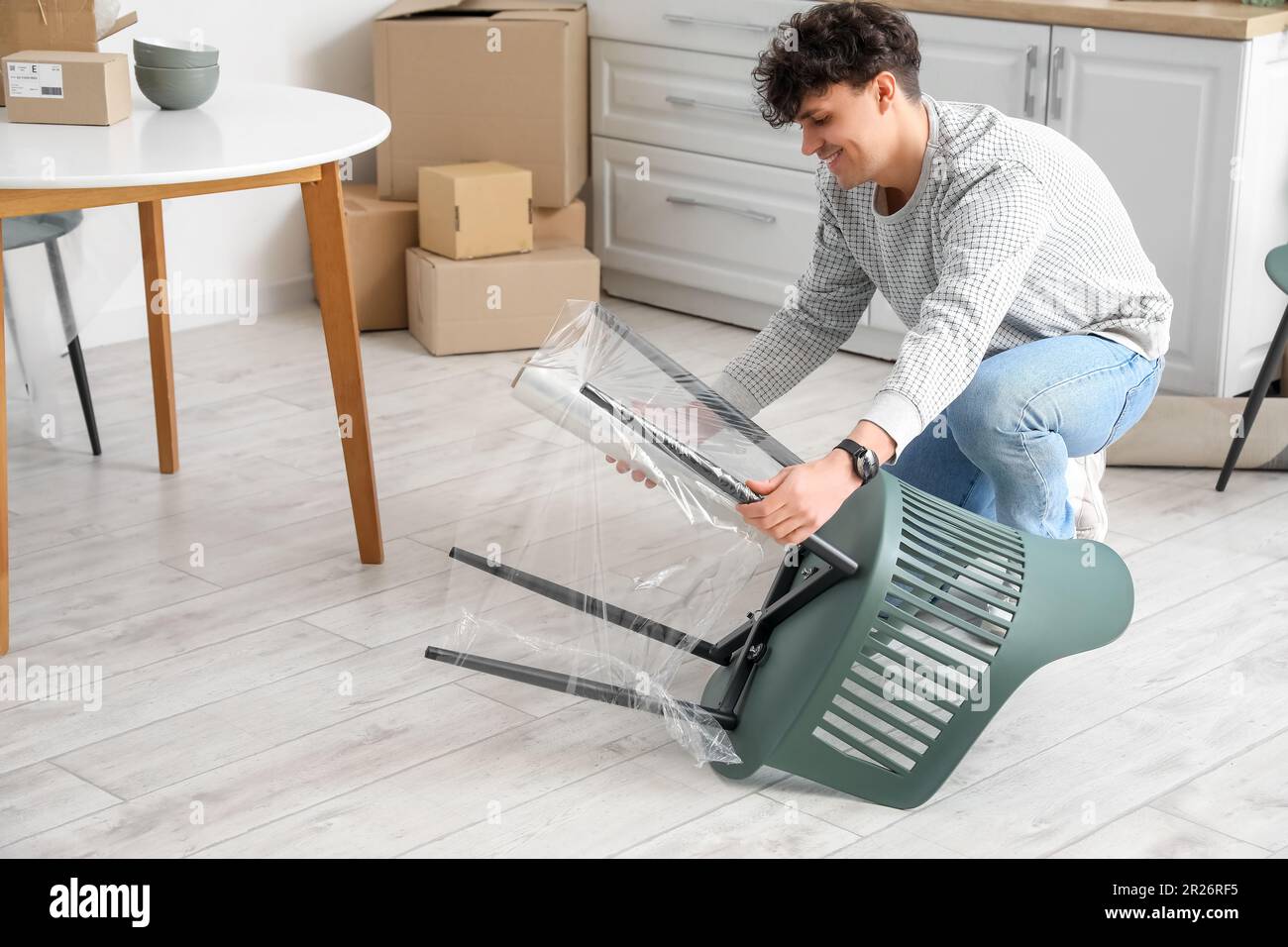Young man wrapping chair with stretch film in kitchen Stock Photo - Alamy