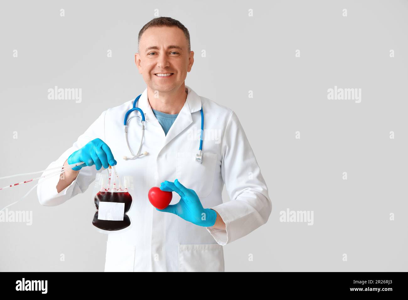 Mature doctor with blood pack for transfusion and heart on light ...