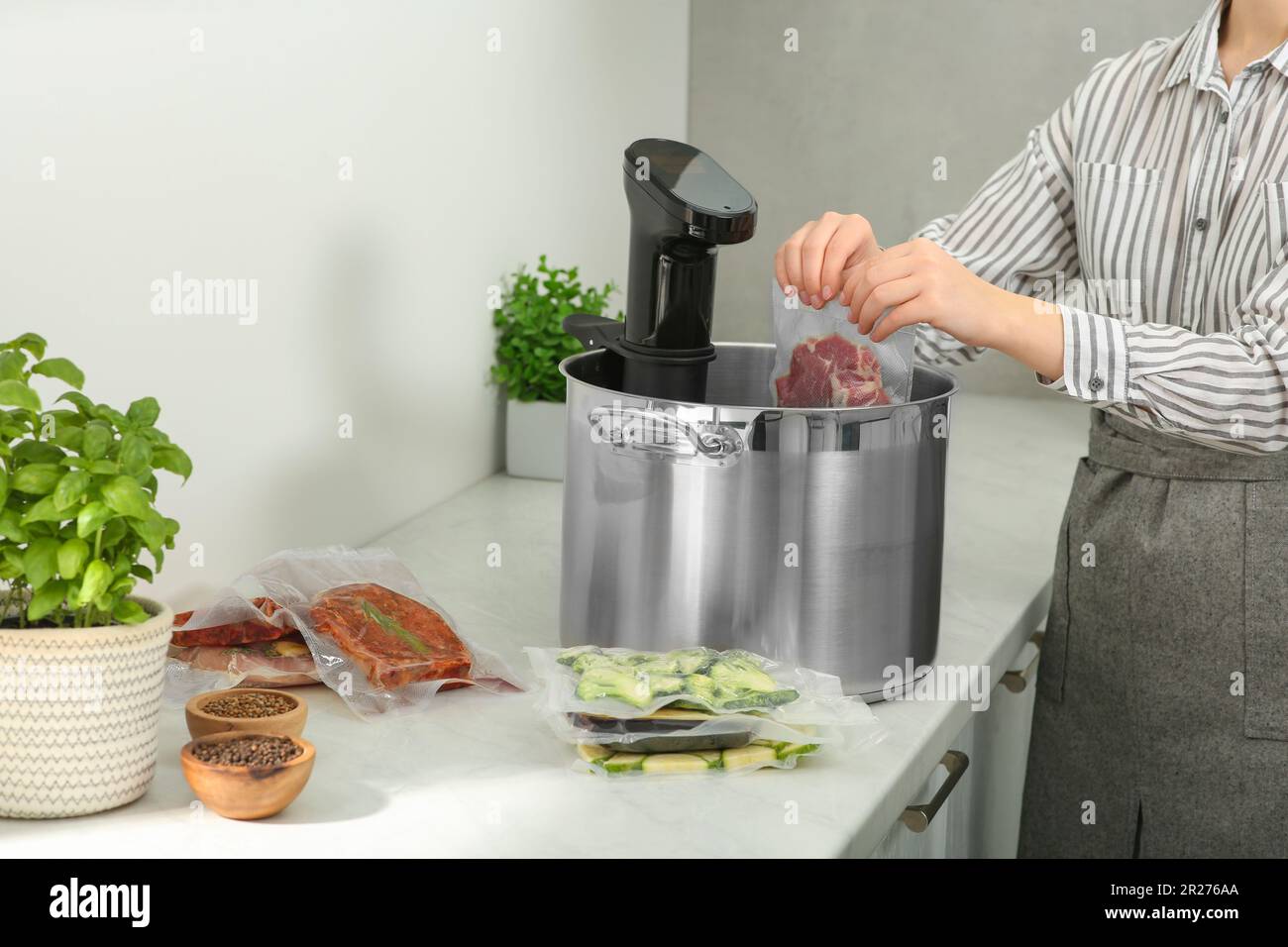 Woman putting vacuum packed meat into pot in kitchen, closeup. Thermal ...