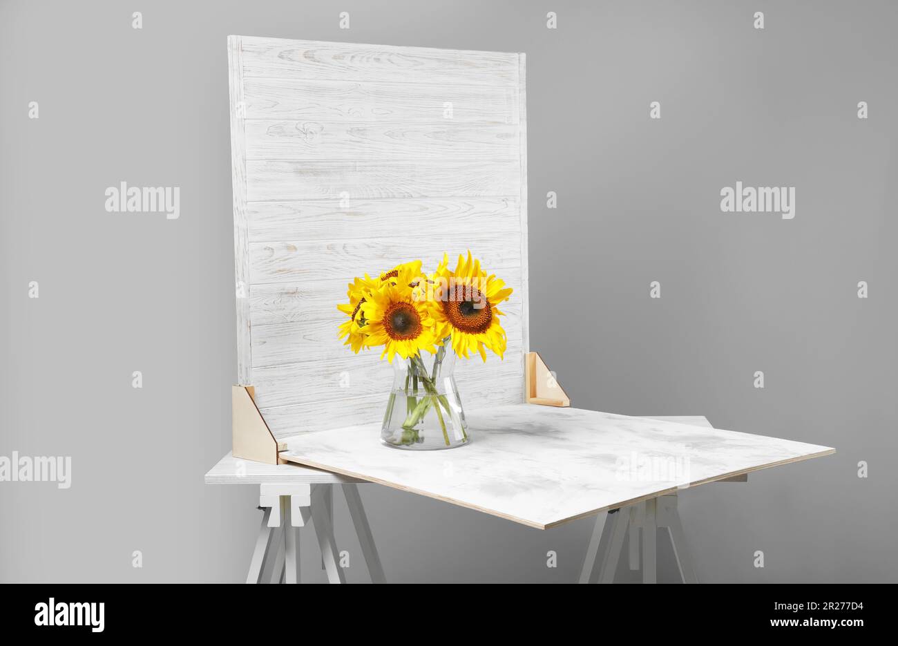 Glass vase with beautiful sunflowers and double-sided backdrop on table ...