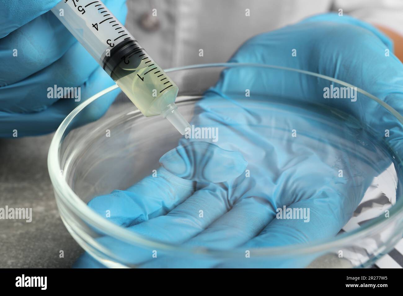 Doctor dripping urine from syringe into petri dish at grey table ...