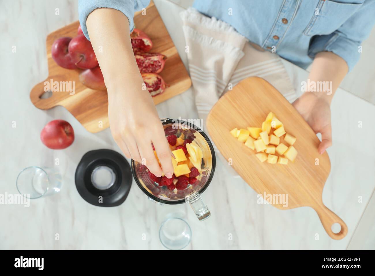 Woman adding mango into blender with ingredients for smoothie at table ...
