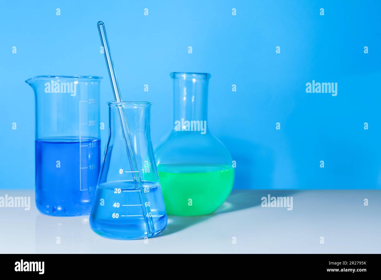 Glass flasks with colorful liquids on white table against light blue ...