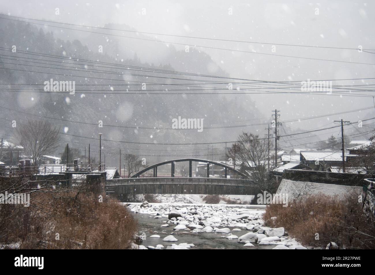 Snow falling on a stone bridge spanning a mountain town Stock Photo - Alamy