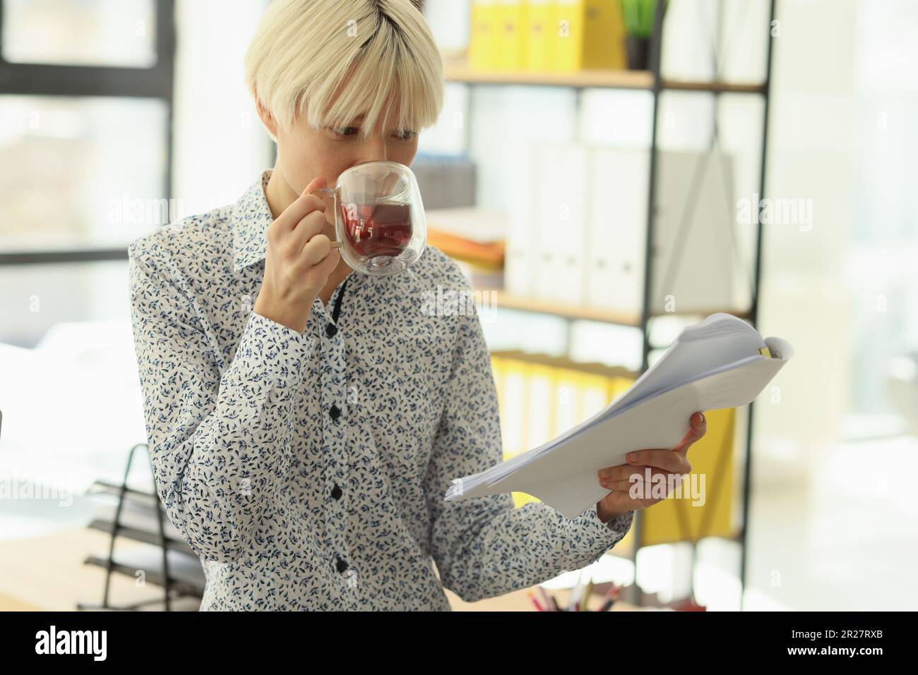 Blonde woman drinks tea in glass cup reading document Stock Photo - Alamy