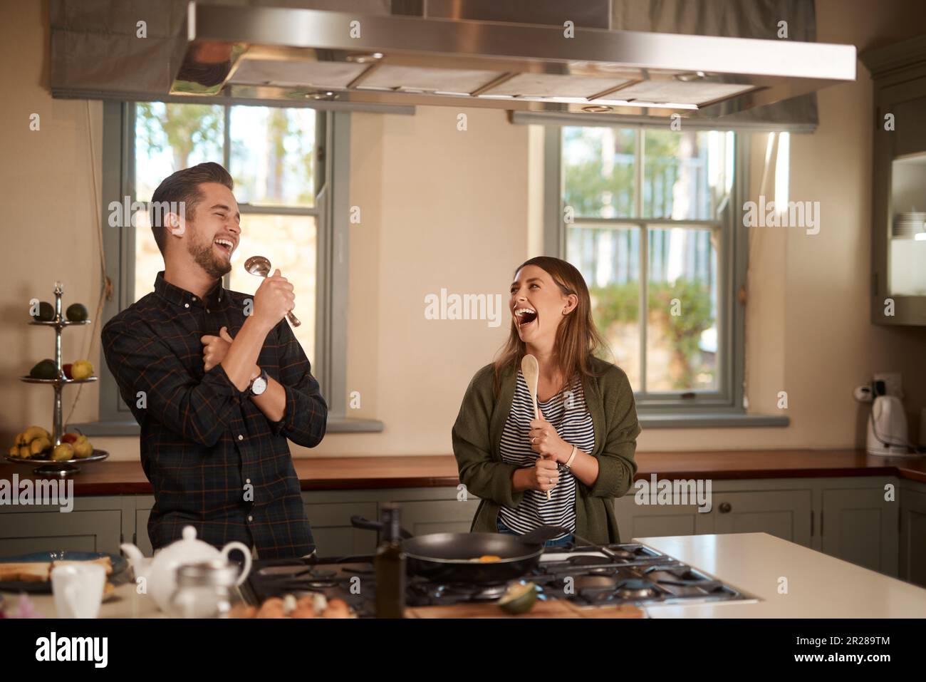 Food, sing and a silly couple in the kitchen of their home, having fun ...