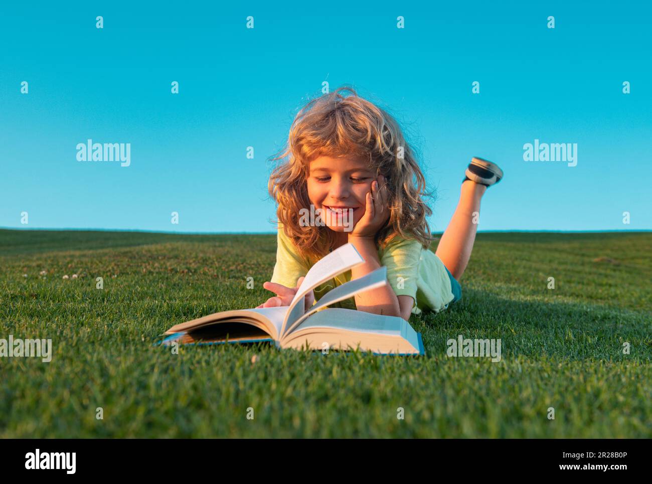 Funny kid reading the book in spring park. Child boy reading book ...