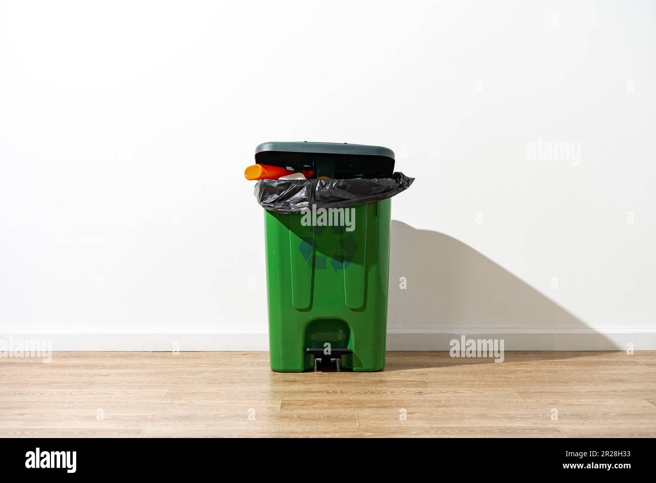 Green plastic trash can full of garbage indoors Stock Photo - Alamy