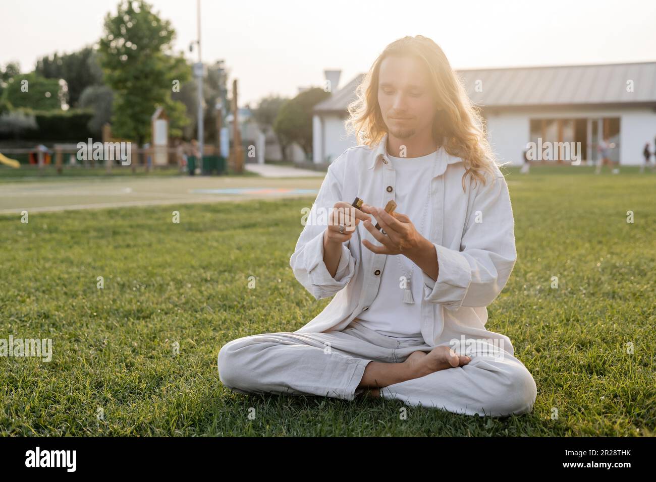 long haired man in white linen clothes sitting in easy yoga pose and ...